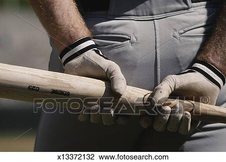 Stock Photo of Baseball player holding baseball bat behind back, close ...