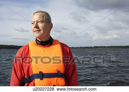 Senior man wearing life jacket by lake Stock Photo | u20227228 | Fotosearch